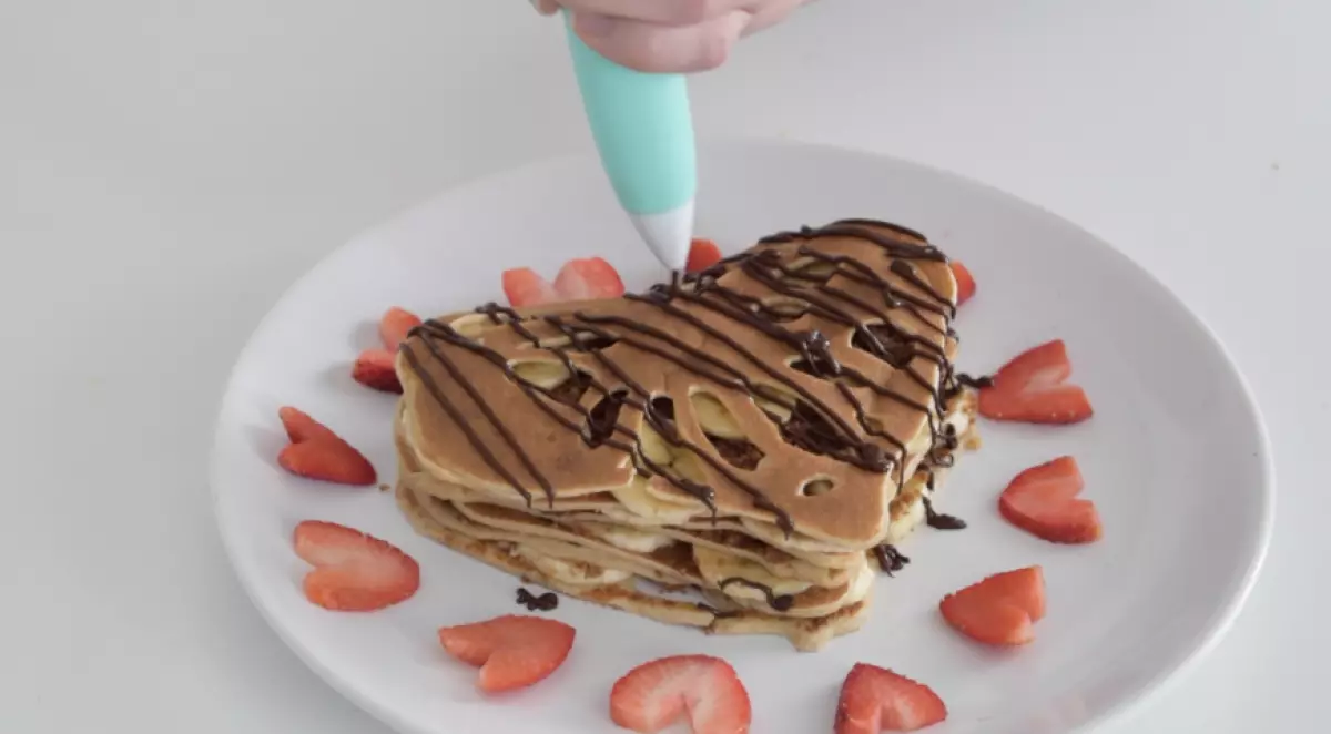 Versare una torta di pancake con le arachidi e la banana scossa cioccolato