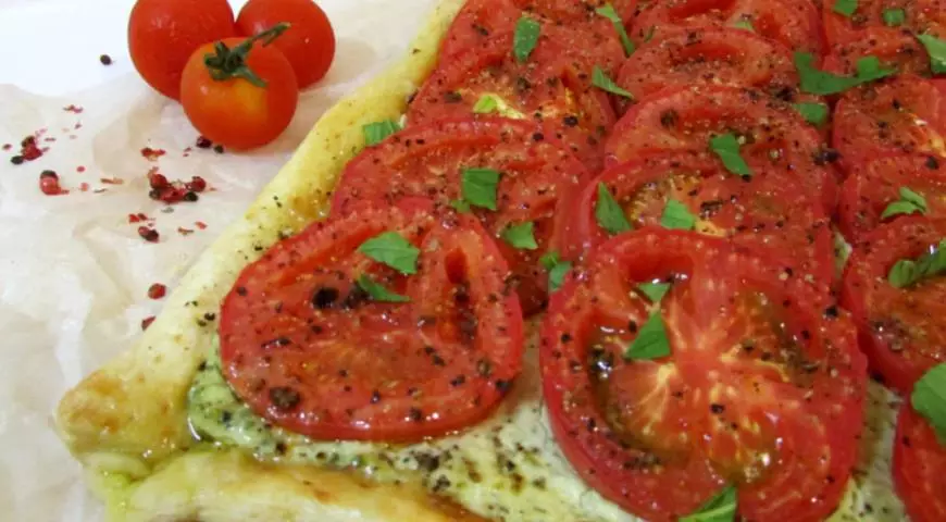 Puff pastry cake with tomatoes, green pesto and basil is ready for feed