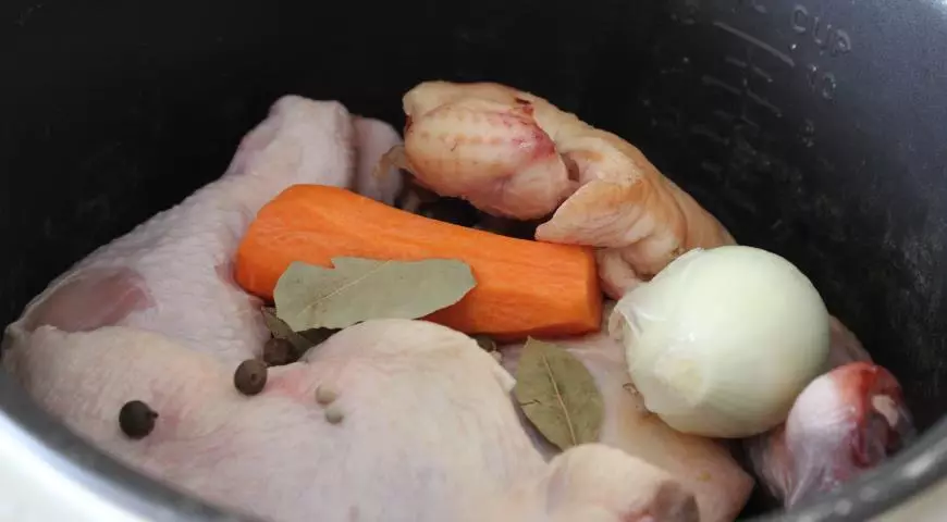 Dalam mangkuk multicooker meletakkan anak ayam ayam, bawang dan wortel