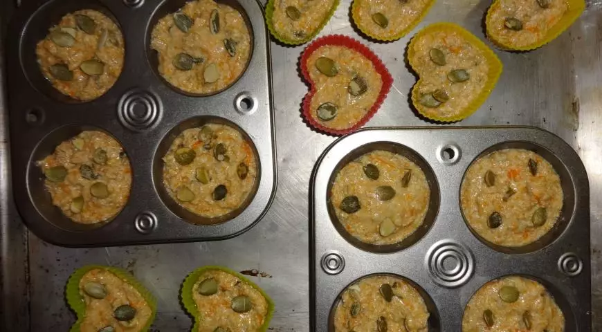 Schmieren Sie die Muffins für Cupcakes, legen Sie den Teig, fügen Sie Kürbiskerne hinzu und legen Sie ihn in den Ofen