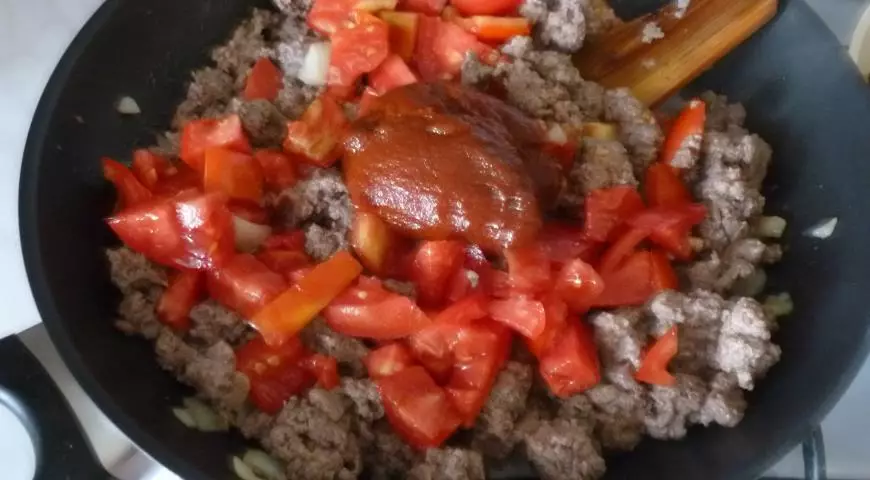 Carne tritata, cipolle e pomodori in una padella, aggiungi pasta di pomodoro