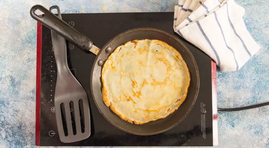 Selbst gemachte dünne Pfannkuchen backen auf einer Gusseisenbratpfanne